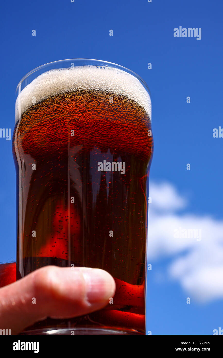 Pint glass of bitter beer in a mans hand held against the background of ...