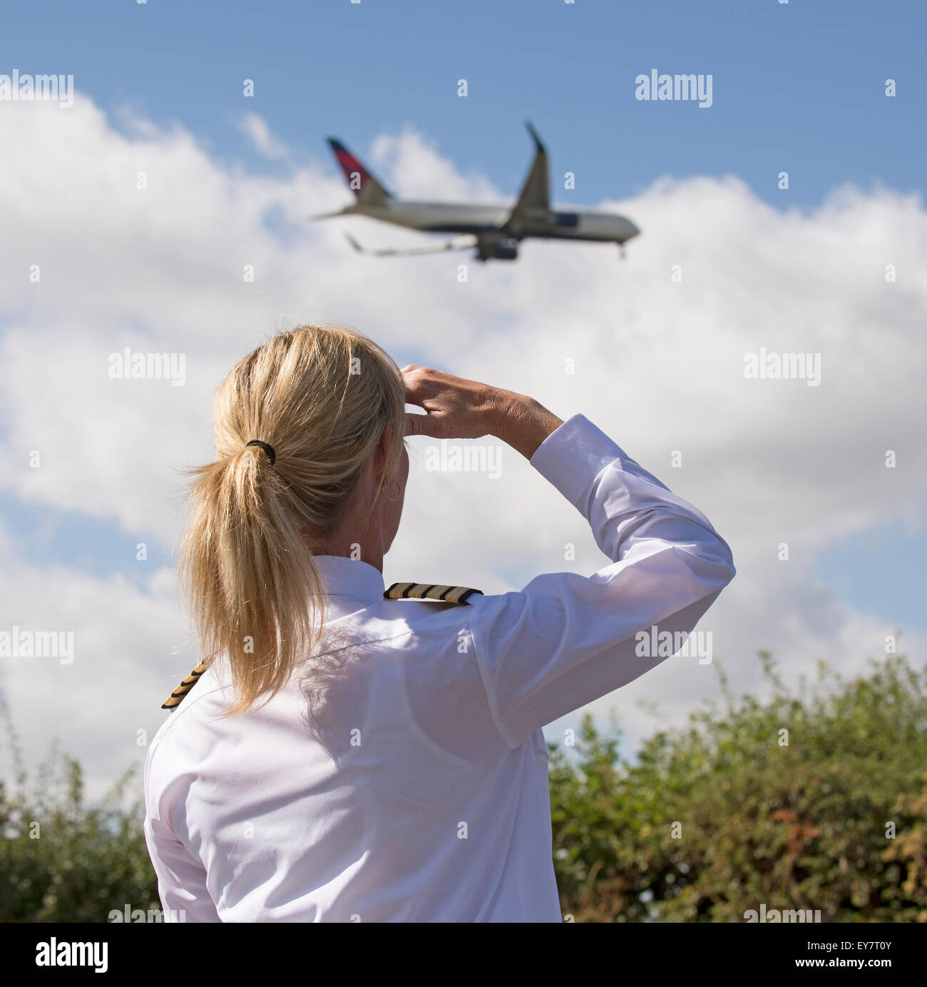 Rear view portrait of a woman pilot with a passenger jet in the sky ...
