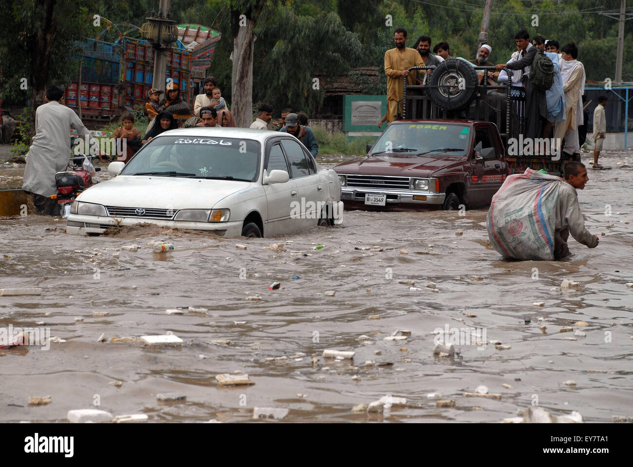 Peshawar. 23rd July, 2015. People and vehicles cross a flooded street ...