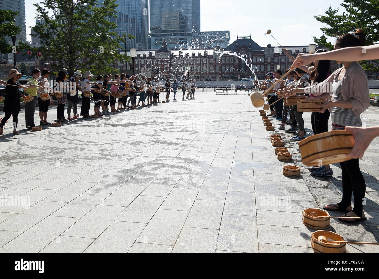Office workers sprinkle water to the pavement during an yoga event held ...