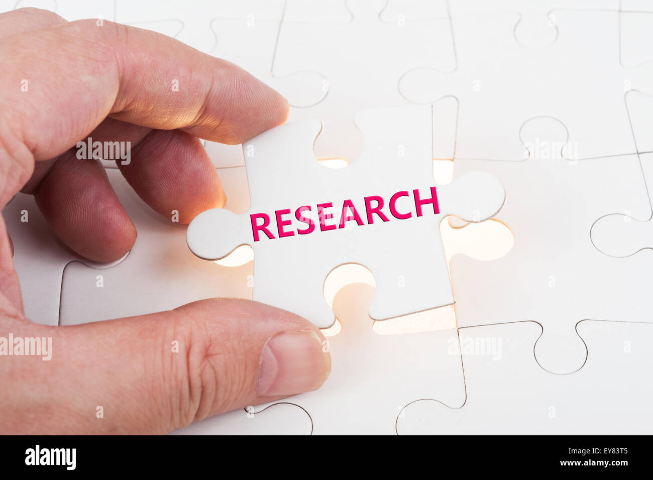 Hand holding puzzle piece which written research word and inserting it ...
