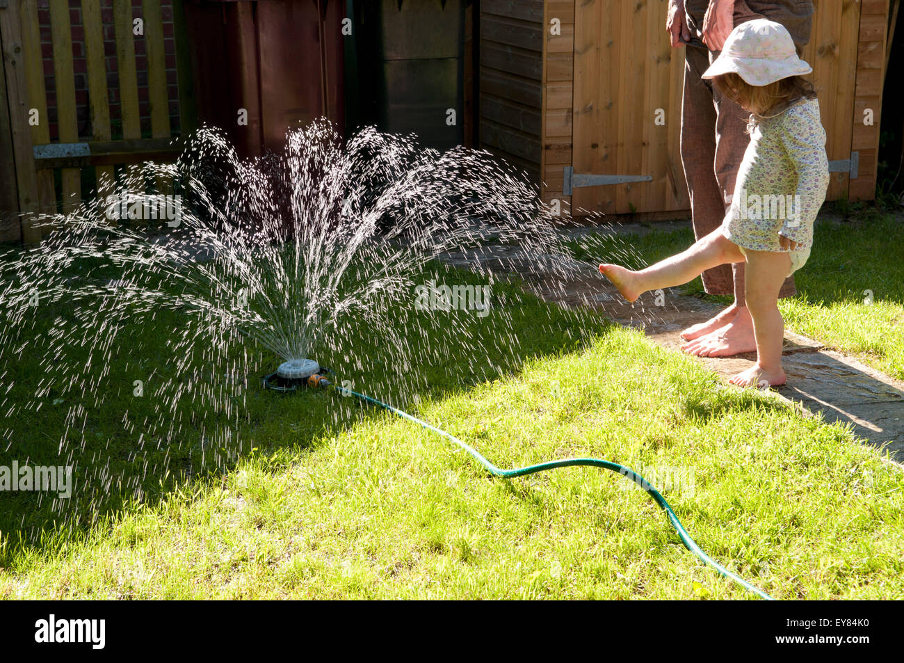 Little girl feeling the water from a garden sprinkler with her foot ...