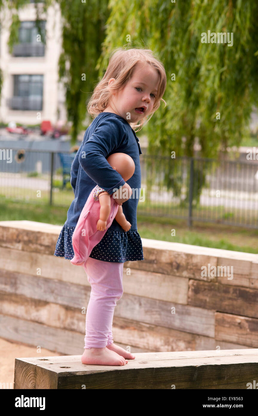 Side view of a little girl standing carrying her doll Stock Photo - Alamy