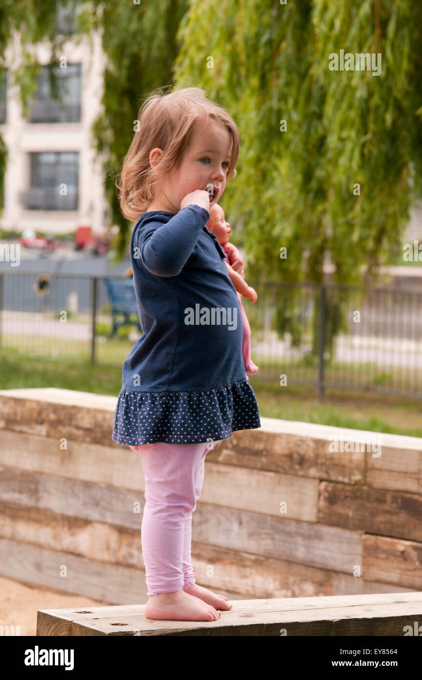 Side view of a little girl standing carrying her doll Stock Photo - Alamy