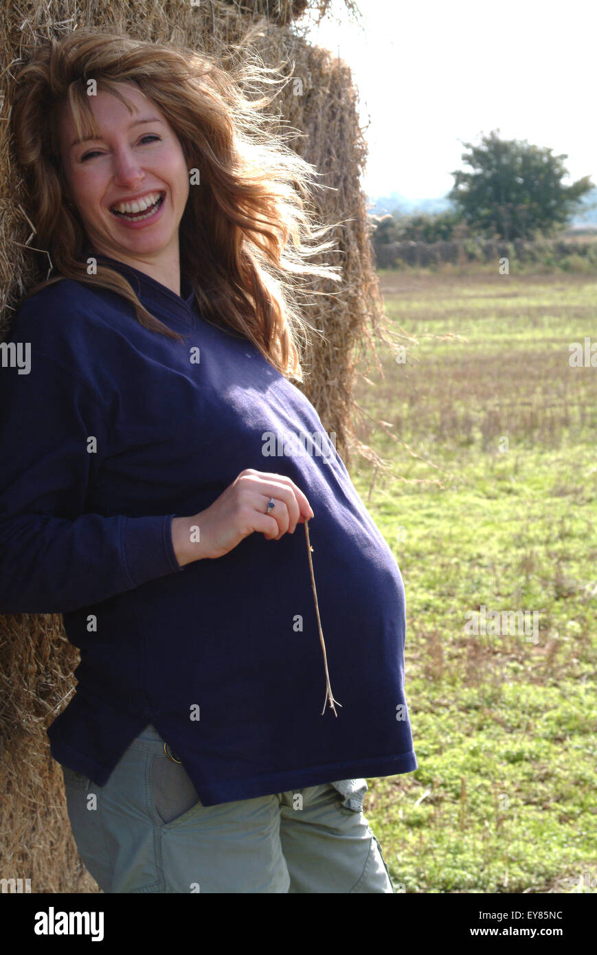 Happy pregnant woman leaning against hay bales Stock Photo - Alamy
