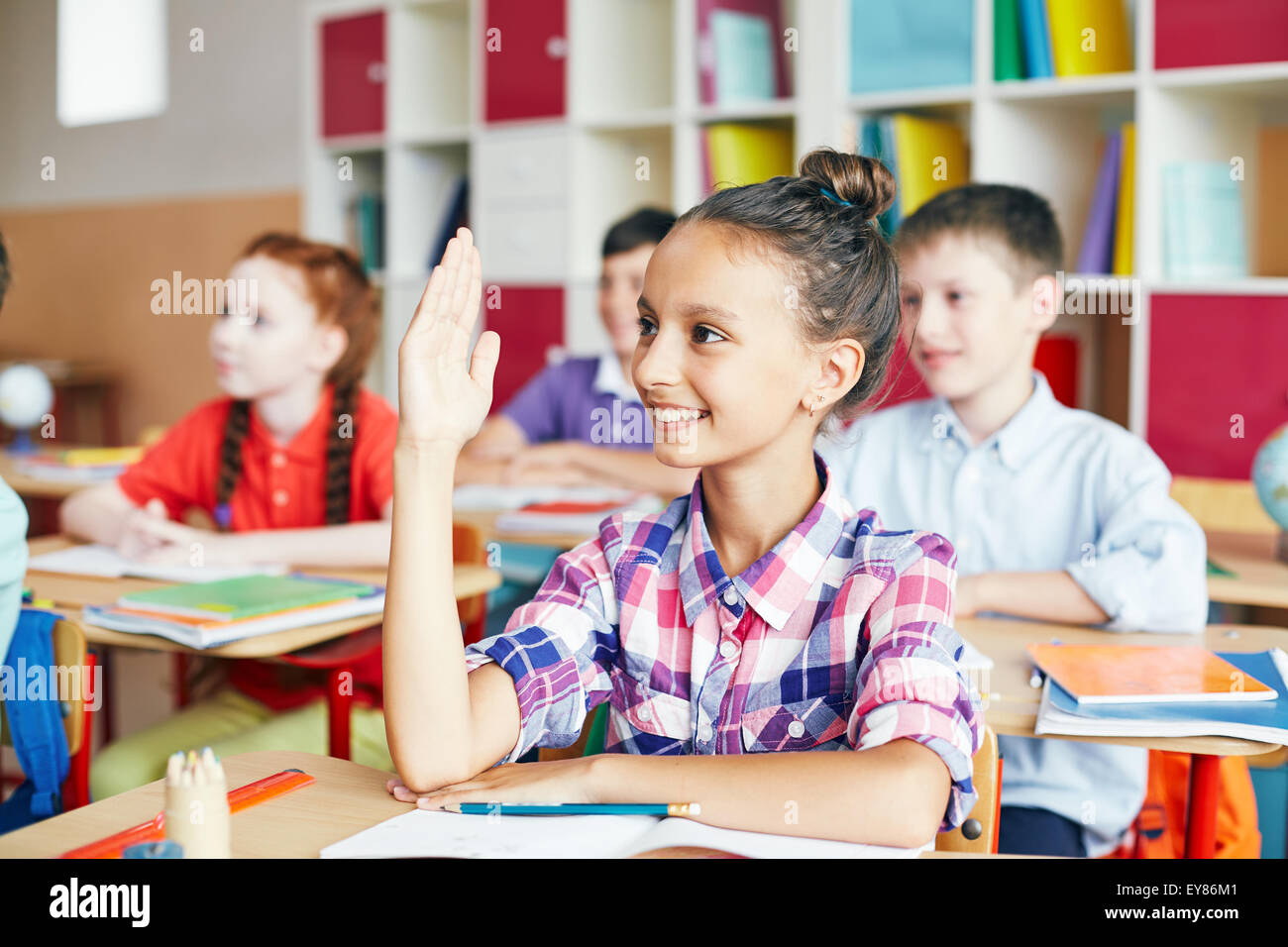 Smiling schoolgirl raising her hand at lesson Stock Photo - Alamy