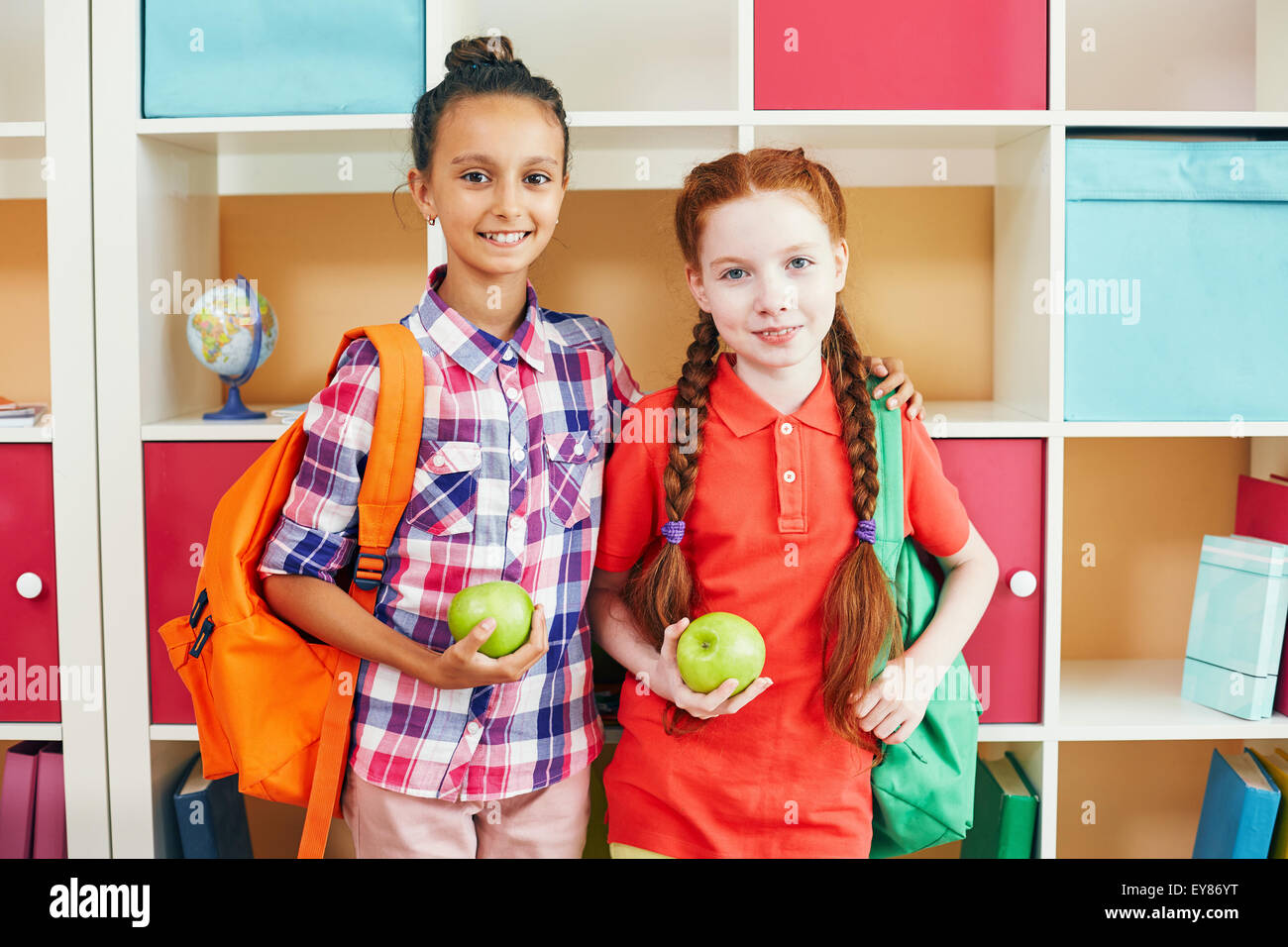 Happy girls with green apples and backpacks looking at camera with ...