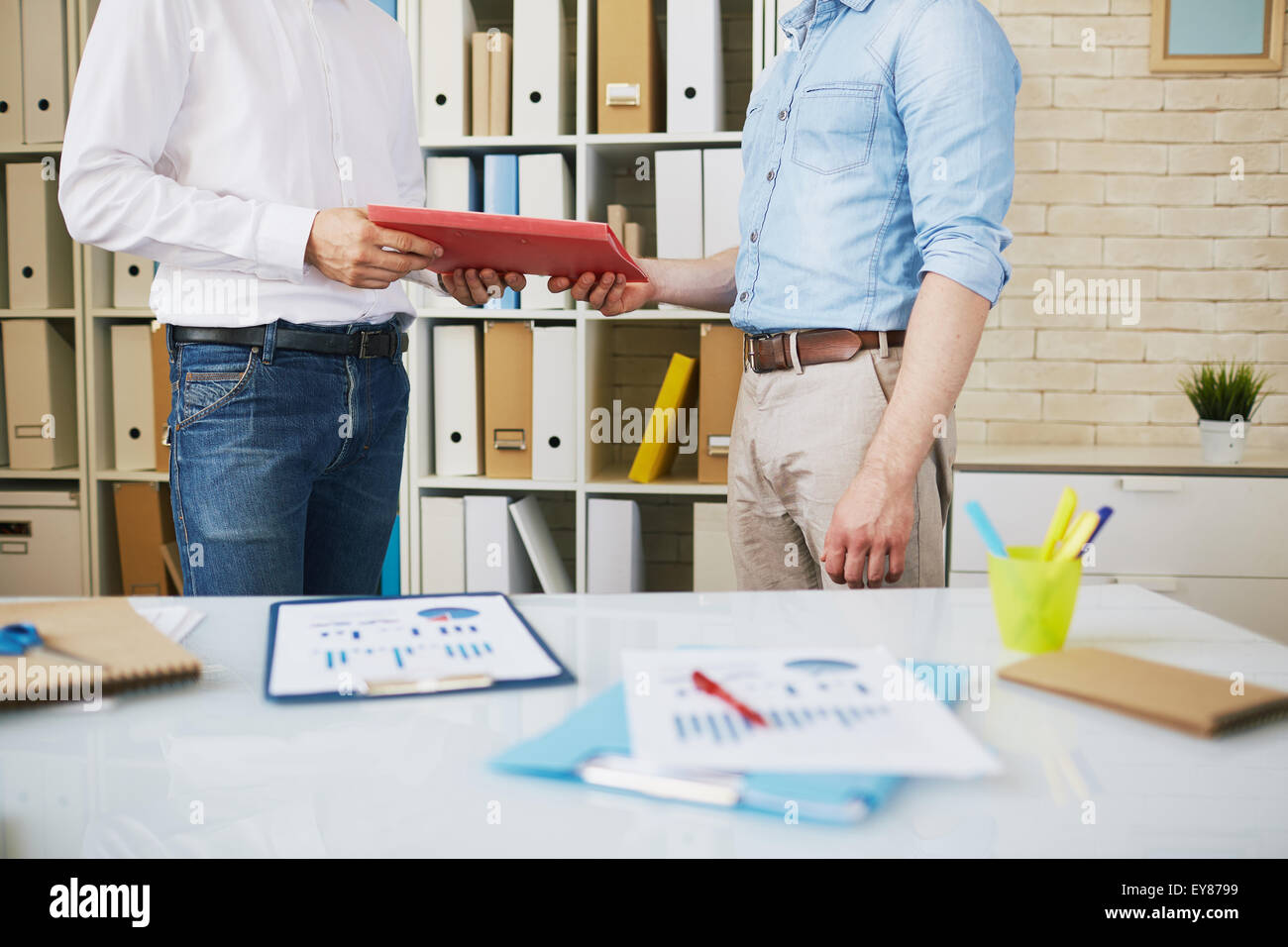Male employee giving clipboard with papers to his colleague in office ...