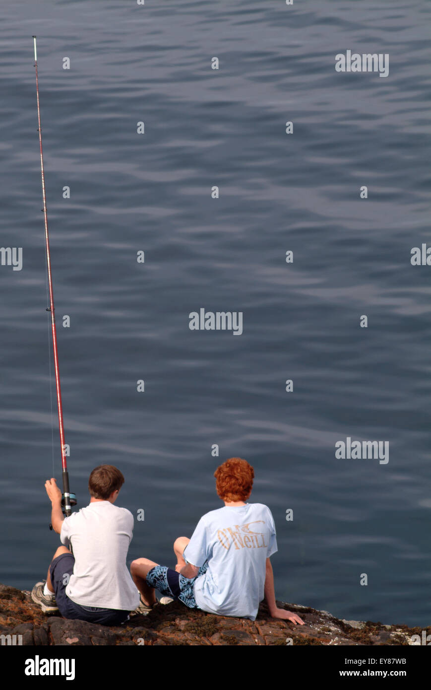 Two teenage boys sitting on rocks, sea fishing Stock Photo - Alamy