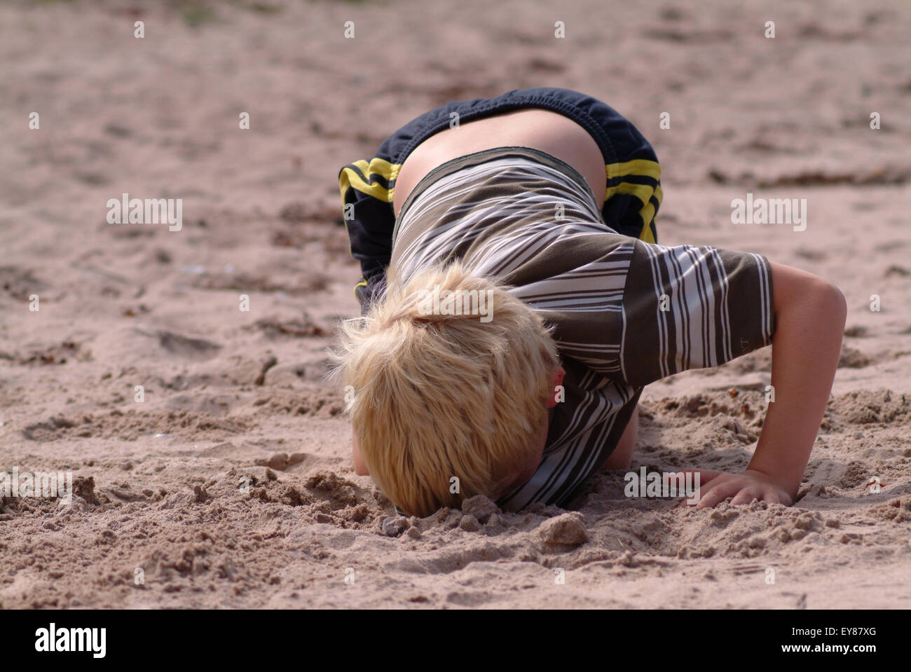 Blonde haired boy digging a deep hole in the sand Stock Photo - Alamy