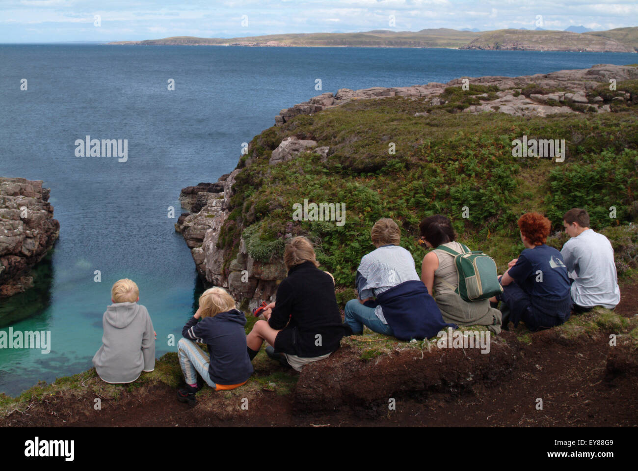 Group of people sitting on a cliff overlooking a small bay Stock Photo ...