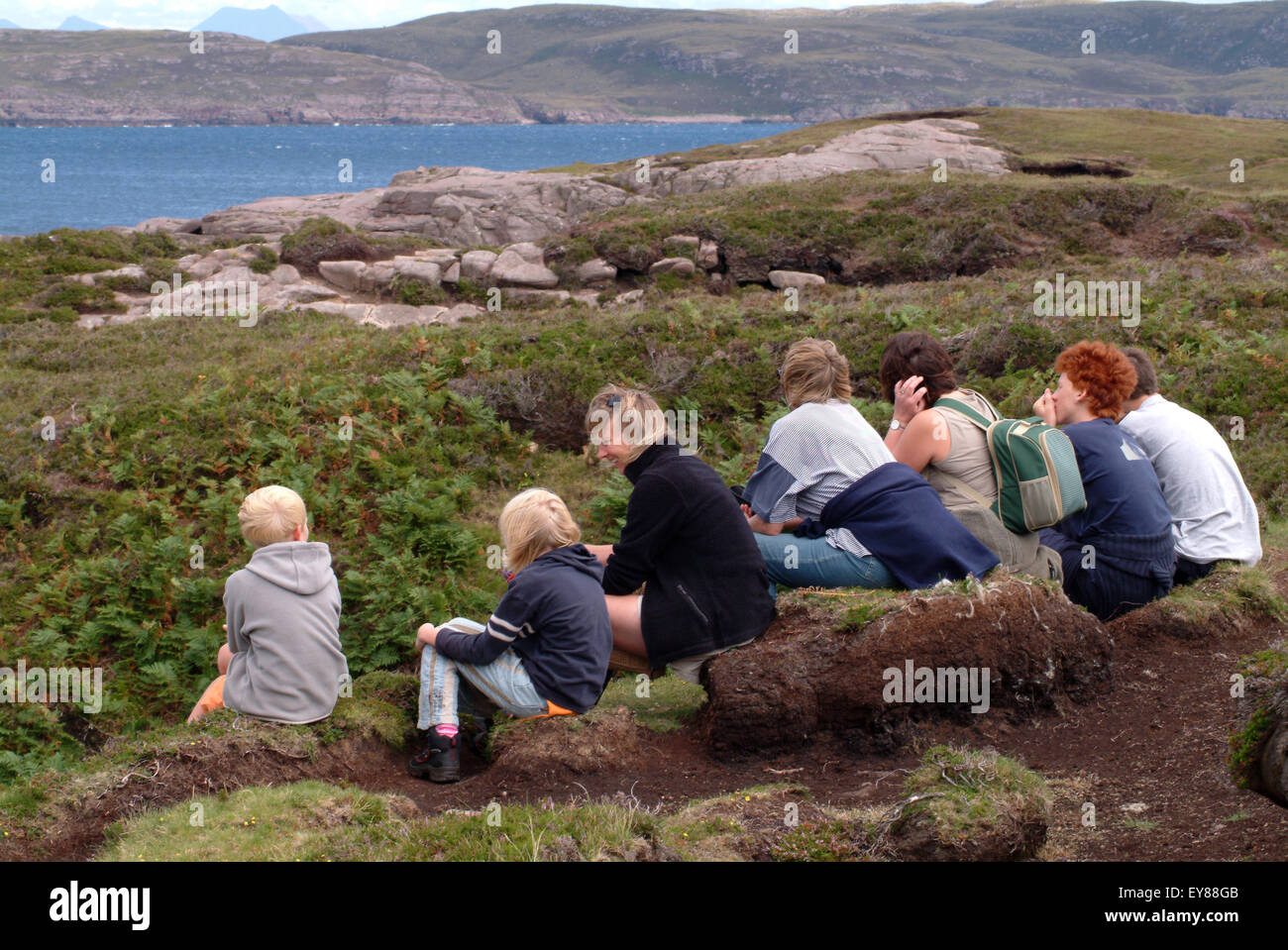 Group of people sitting on a cliff overlooking a small bay Stock Photo ...