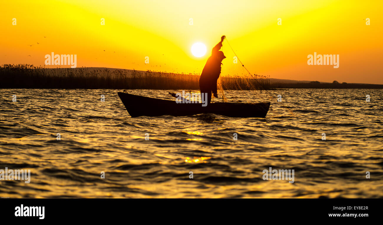 Sunset in Romania Fisherman casting net at sunset over tranquil waters ...