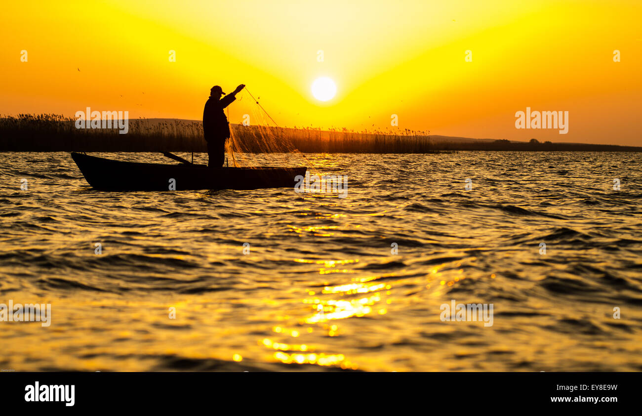 Sunset in Romania Fisherman casting net at sunset over tranquil waters ...