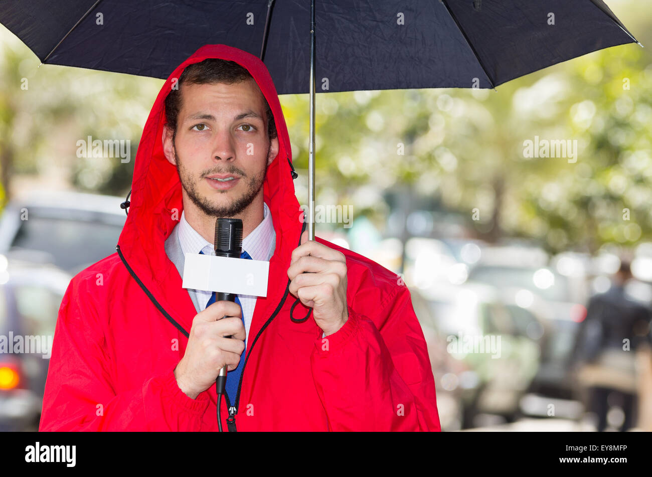 Successful handsome male journalist wearing red rain jacket working in ...