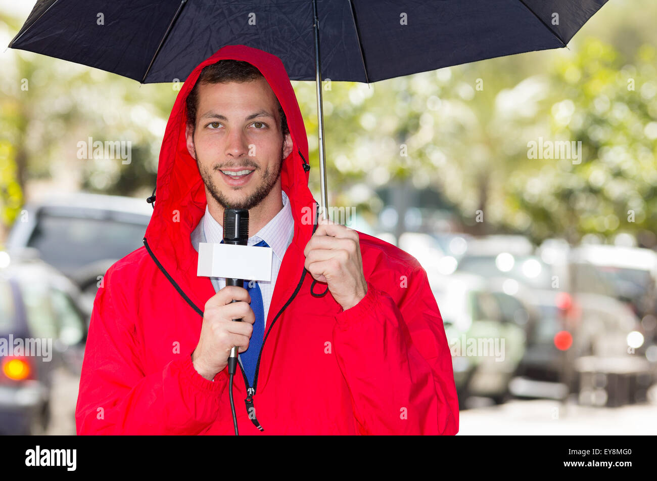 Successful handsome male journalist wearing red rain jacket working in ...