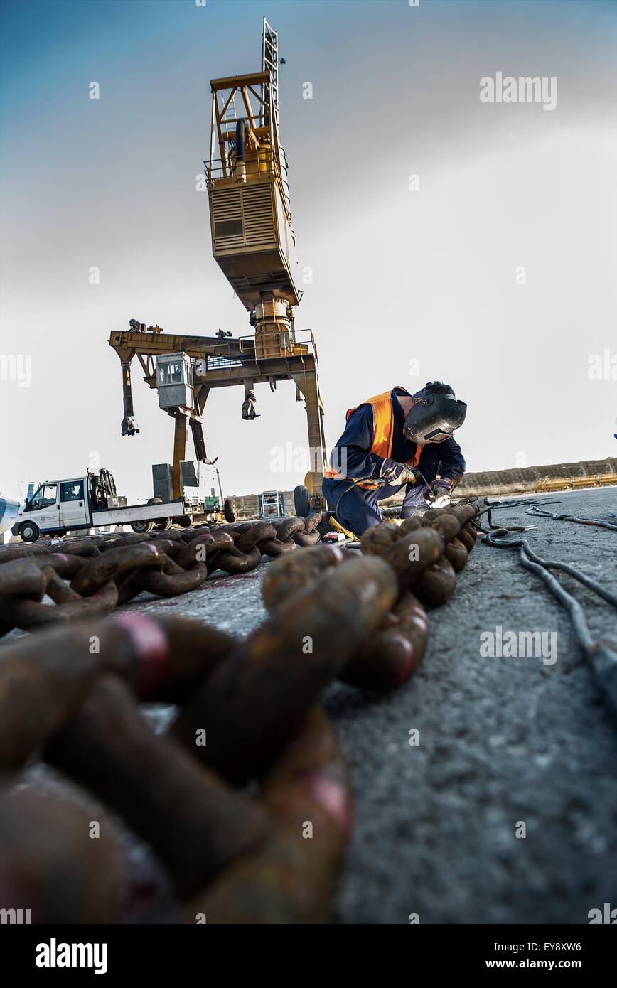 Welder welding chain on dock pier Stock Photo - Alamy