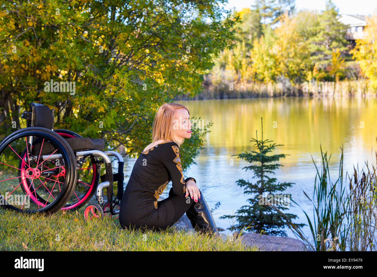 Young paraplegic woman beside her wheelchair by water in a city park in ...