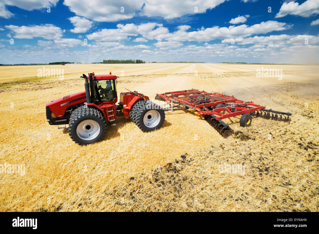 A tractor pulling a disc harrow works soil containing barley stubble ...