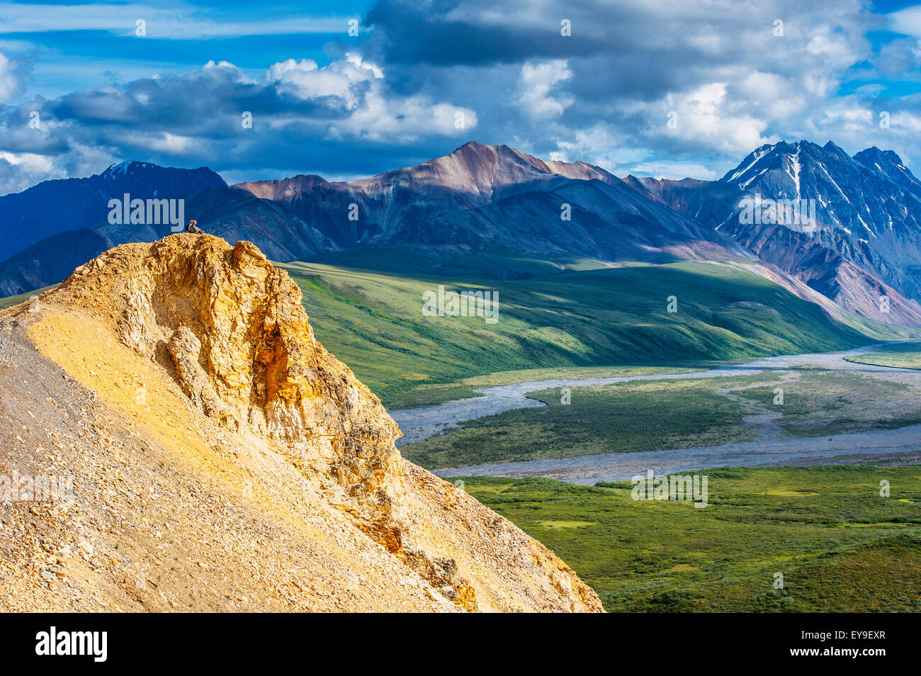 A couple sitting on a rock ledge taking in the view at Polychrome Pass ...