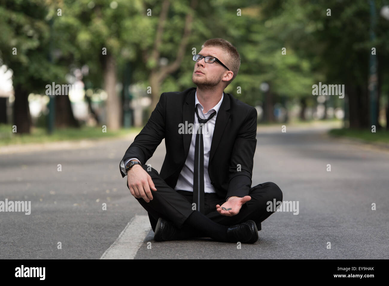 Young Businessman Sitting on Asphalt Begs For Money Outdoors In Park ...