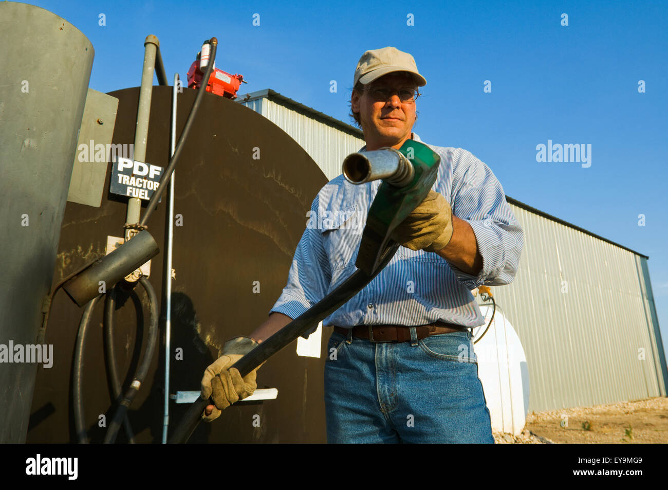 Agriculture - A farmer holds a fuel nozzle at the farm fuel tank ...