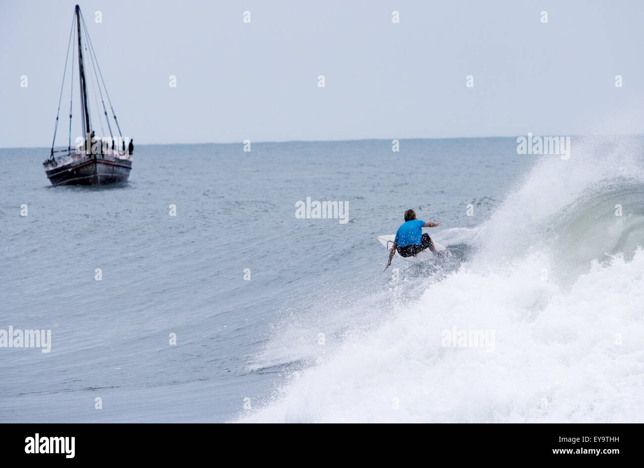 Surfer Riding Wave With Sailboat Behind Stock Photo - Alamy