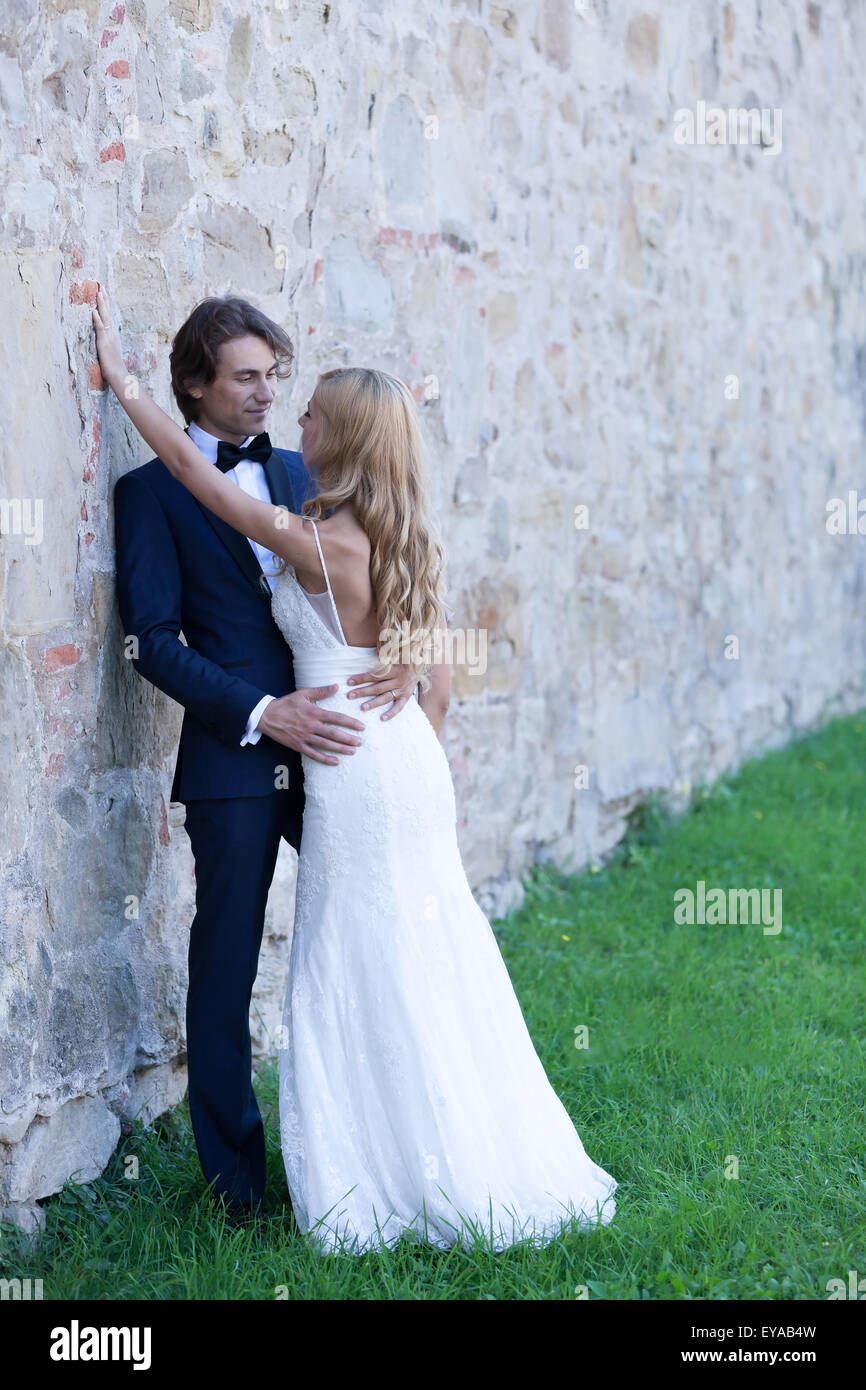 Romantic married couple sharing looks full of love, leaning at a wall ...