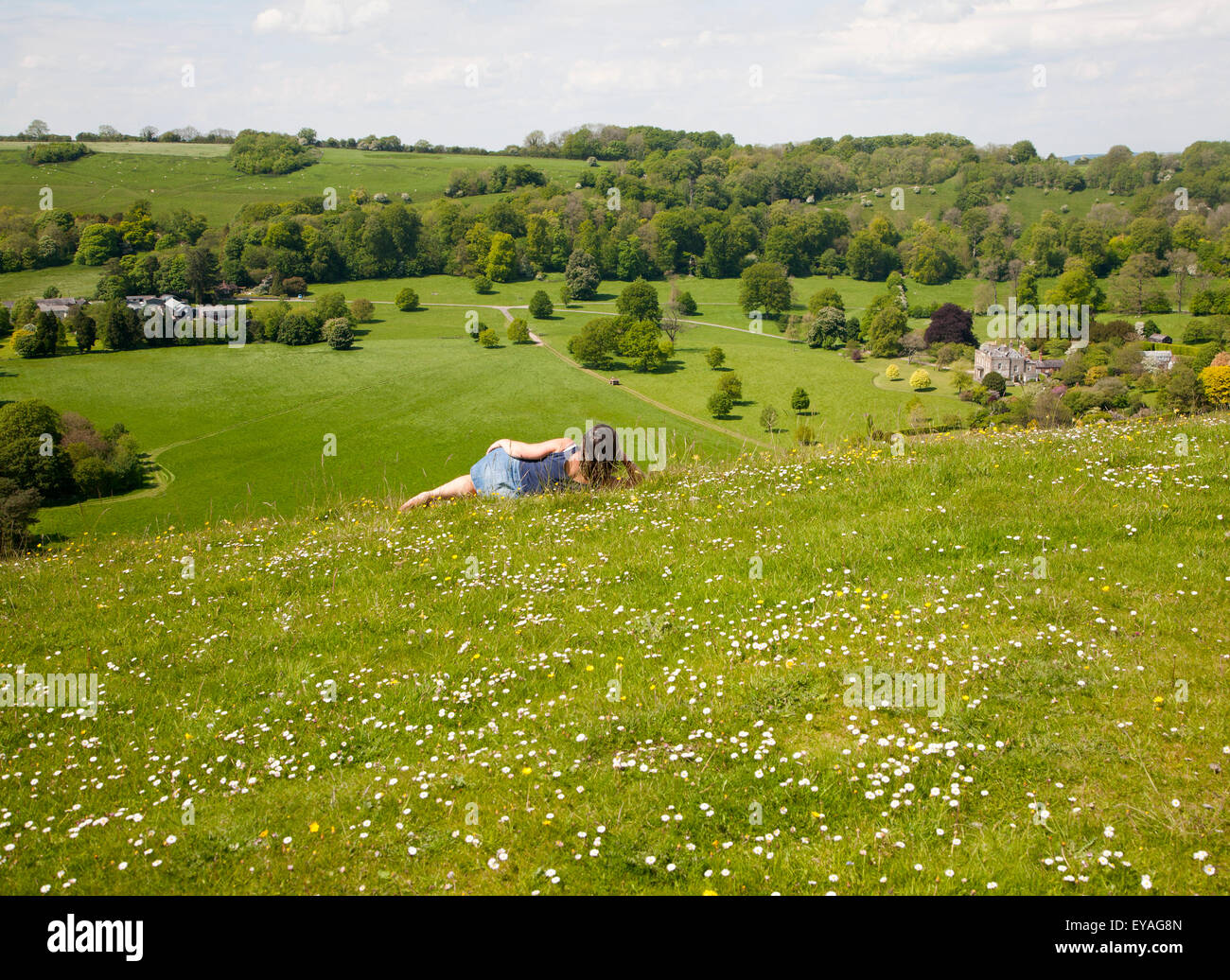 Woman lying on chalk grassland looking into deep green valley ...