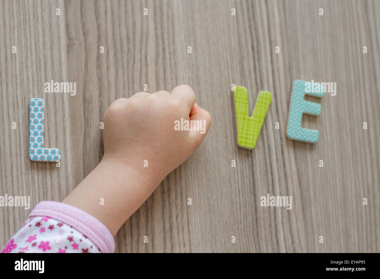 Child is writing word "Love" with colorful toy letters on a wooden ...