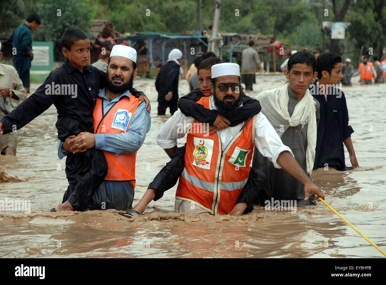 Peshawar. 26th July, 2015. Rescuers hold children in a flooded area in ...