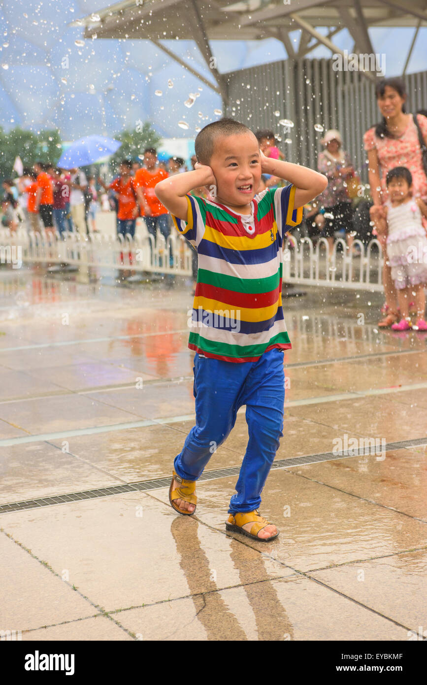 Chinese boy enjoying playing among the water-sprinklers at the Olymoic ...