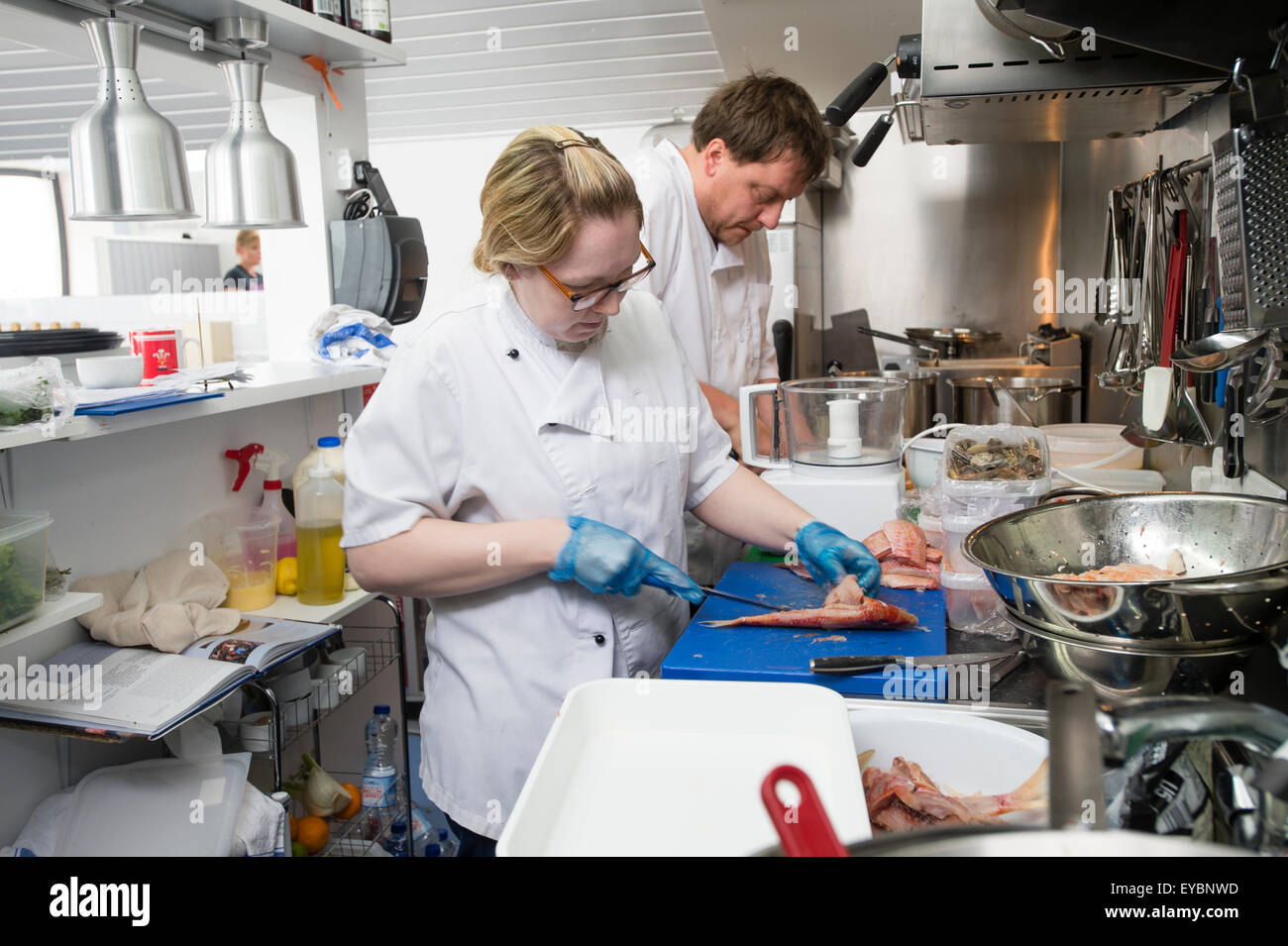 Two chefs - man and woman - working preparing fresh fish in the kitchen ...