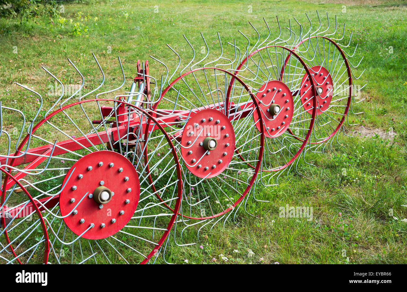 New hay tedder on a green meadow with flowers. Close-up Stock Photo - Alamy