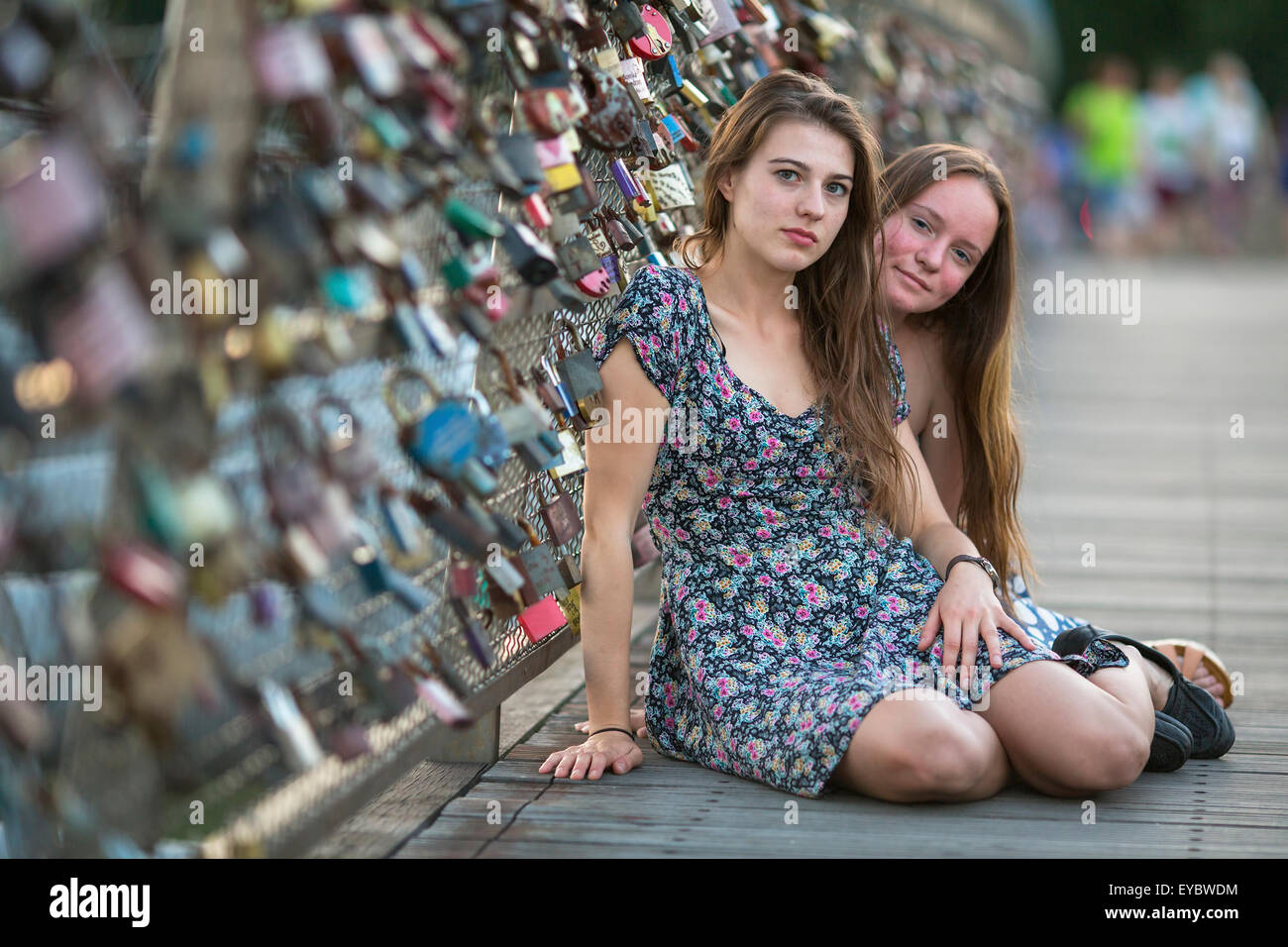Two young cute girls girlfriend sitting on the bridge of love with ...