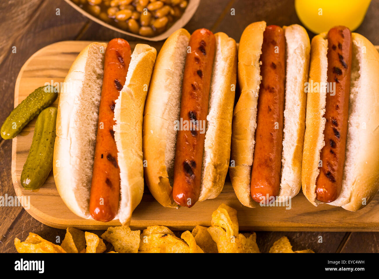 Grilled hot dogs on a white hot dog buns with chips and baked beans on ...