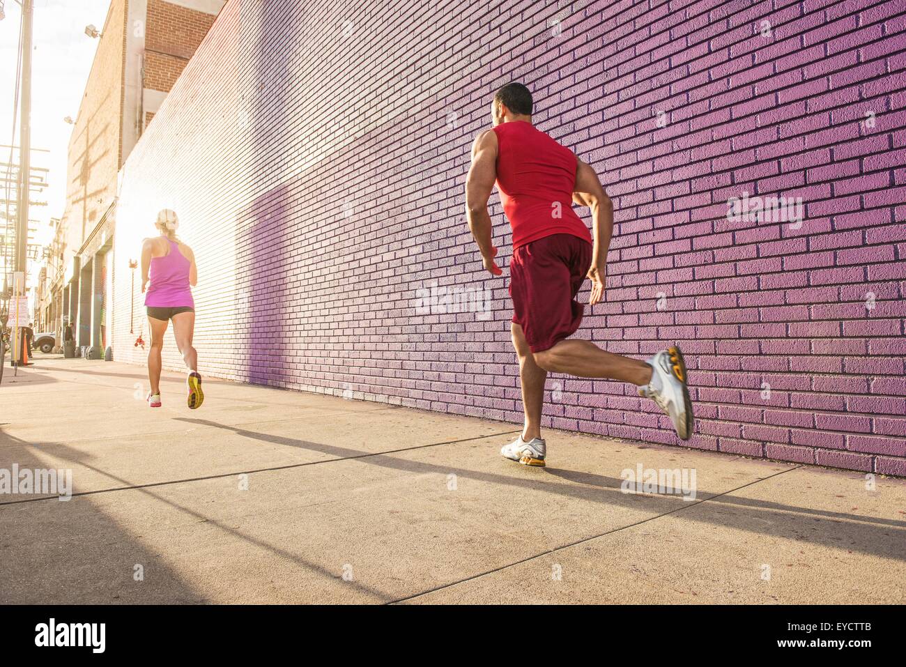 Rear view of male and female runners running along sidewalk Stock Photo ...