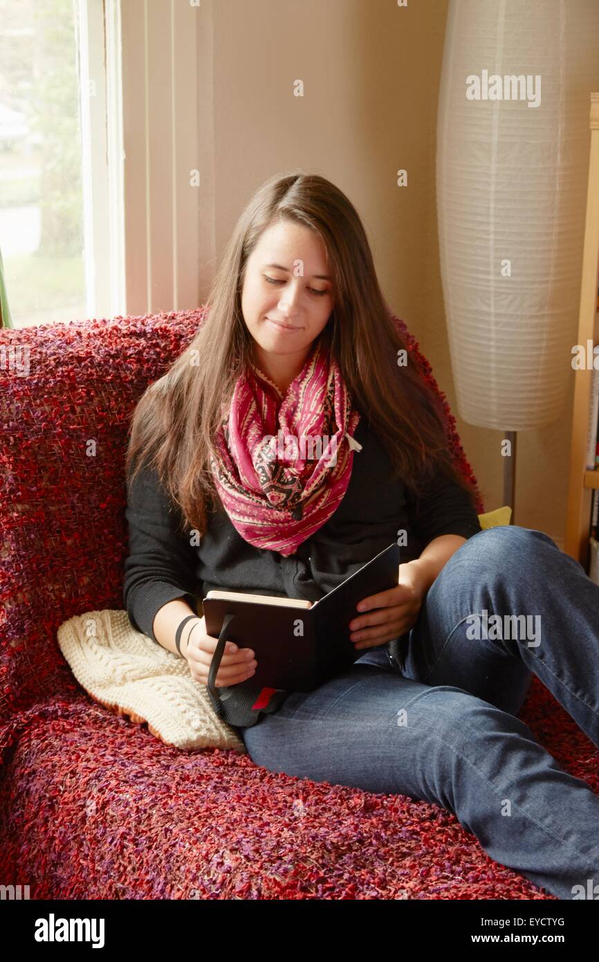 Young woman reclining on sofa reading a book Stock Photo - Alamy