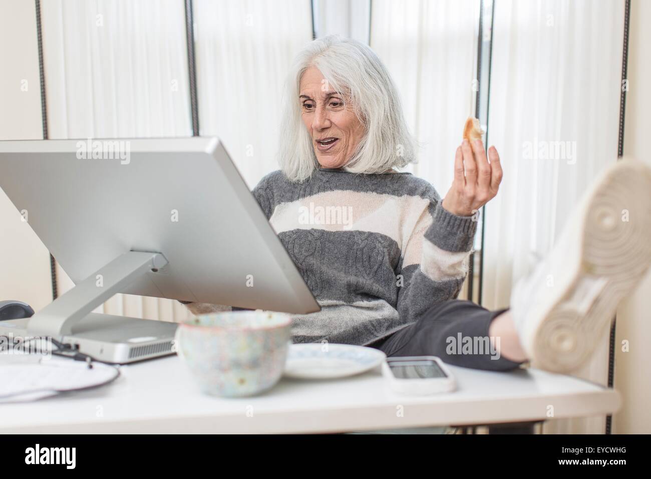 Portrait of senior woman sitting at computer with foot on desk Stock ...