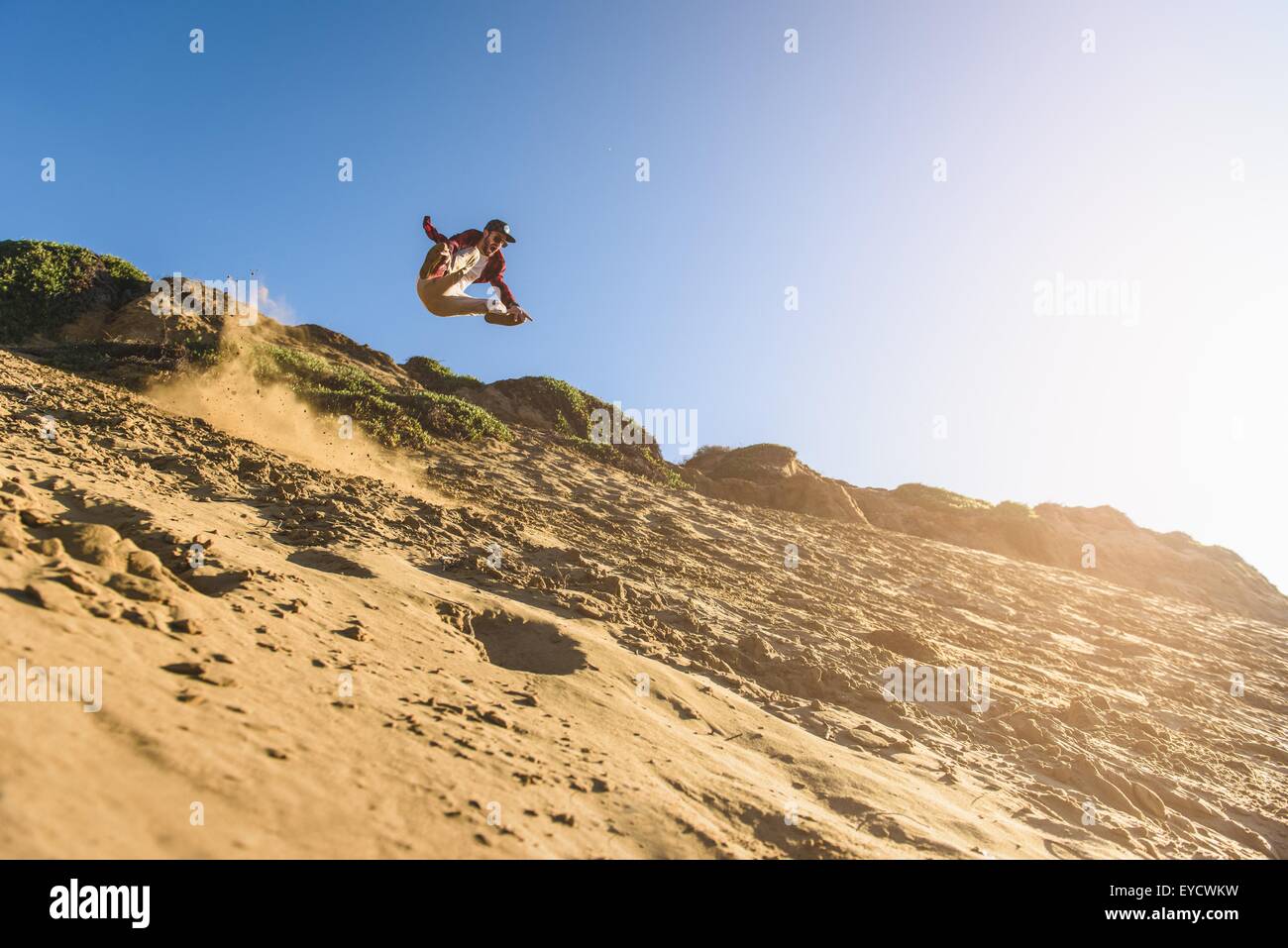Young man jumping down sandy hill, in mid air Stock Photo - Alamy