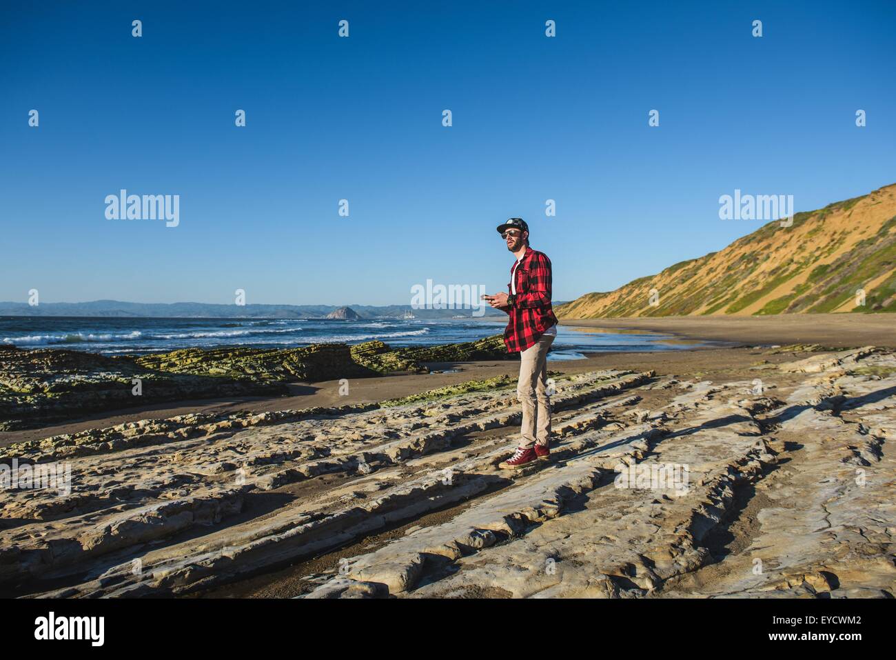 Young man standing on beach looking at ocean Stock Photo - Alamy