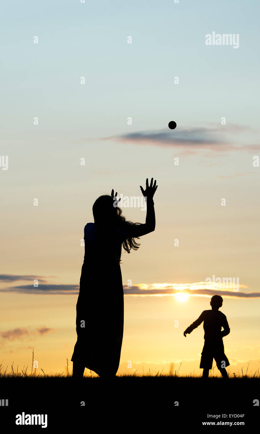 Young girl and boy playing catch with a ball at sunset. Silhouette ...