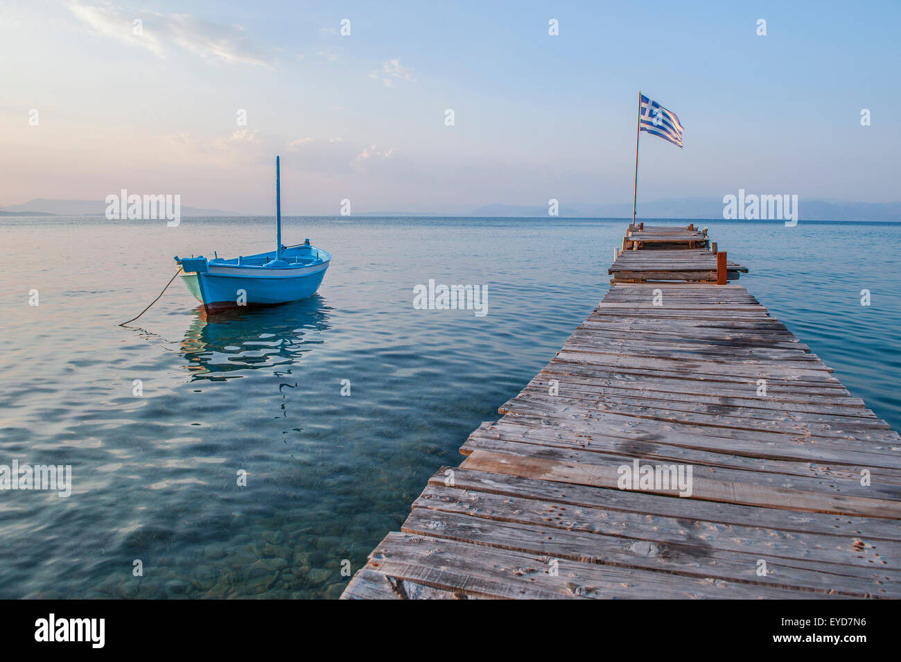 A small Greek fishing boat by a jetty with a Greek flag in the Greek ...