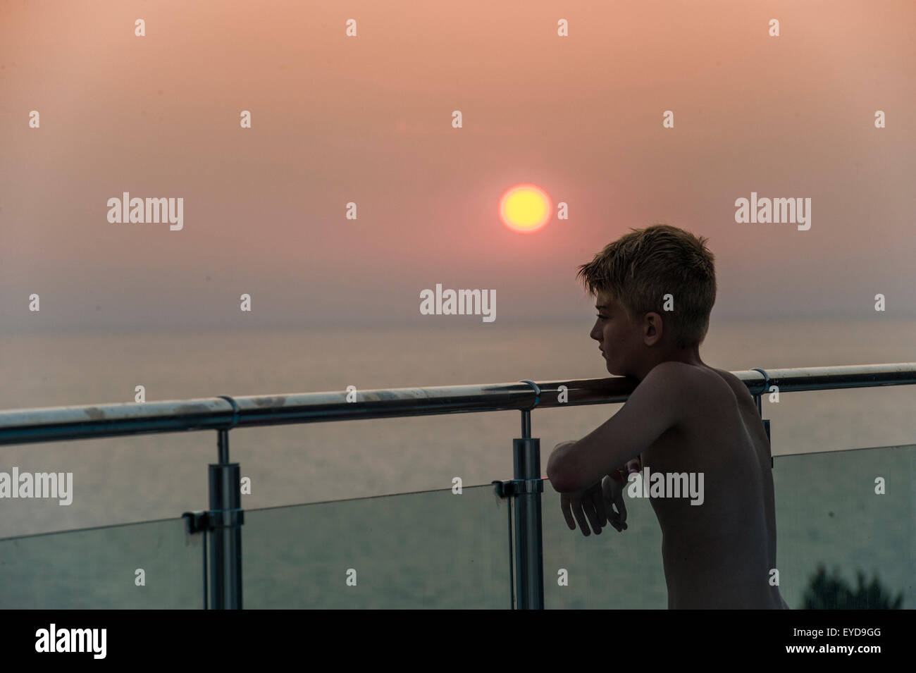 A boy watches the sun set from a glass wall on holiday Stock Photo - Alamy