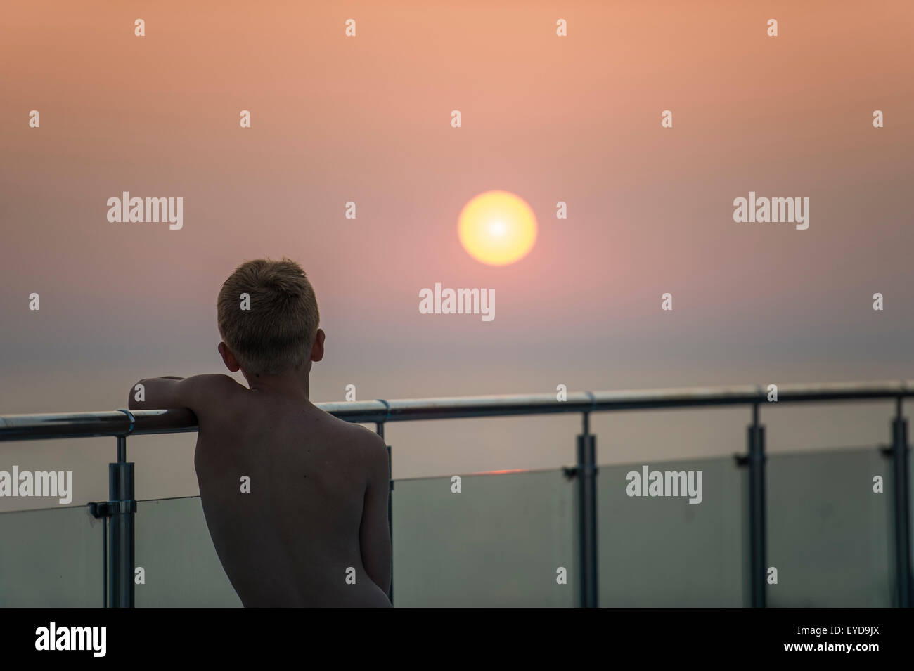 A boy watches the sun set from a glass wall on holiday Stock Photo - Alamy