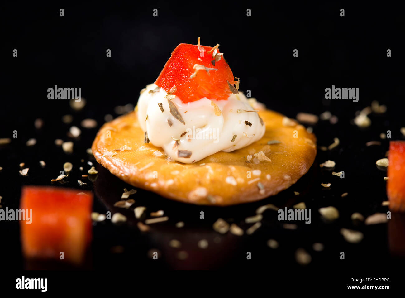 One Cracker with Cream Cheese and red bell pepper over black background ...