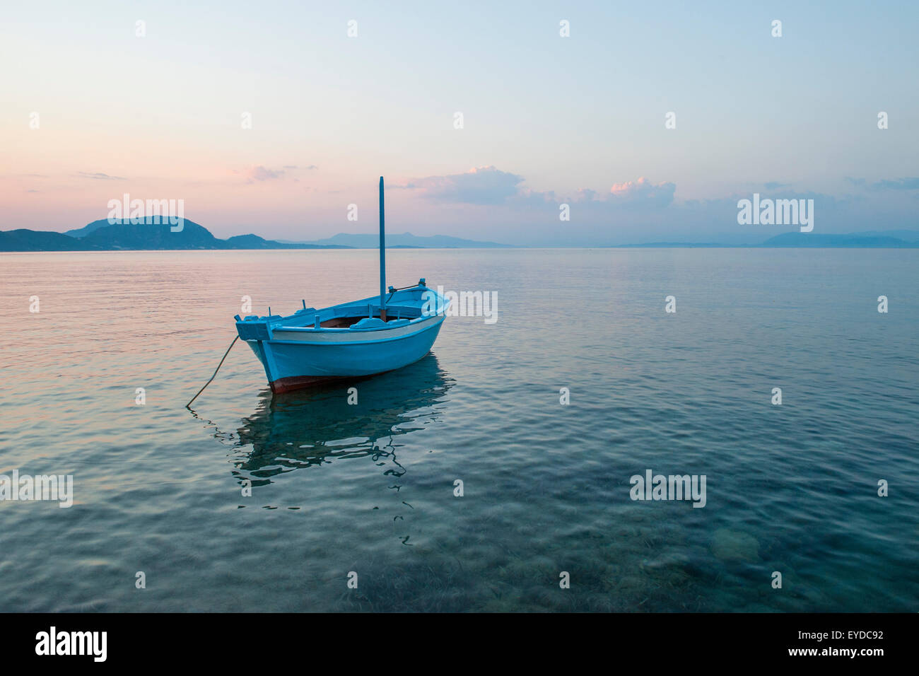 A small Greek fishing boat in a calm sea at sunset in the Greek Islands ...
