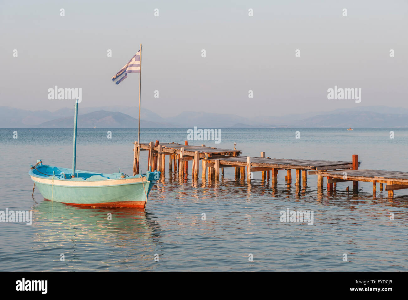 A small Greek fishing boat by a jetty with a Greek flag in the Greek ...