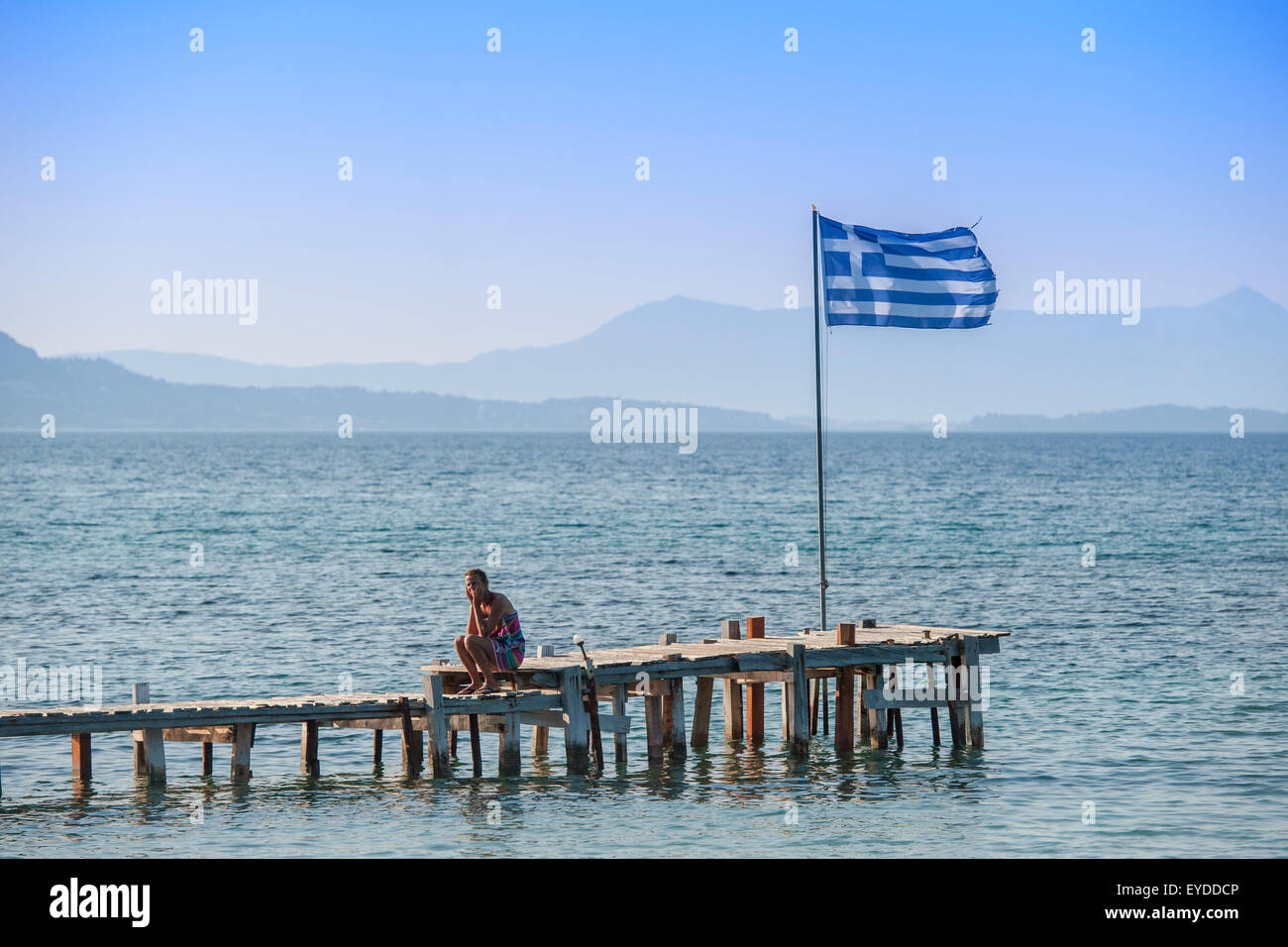 A small Greek fishing boat by a jetty with a Greek flag in the Greek ...