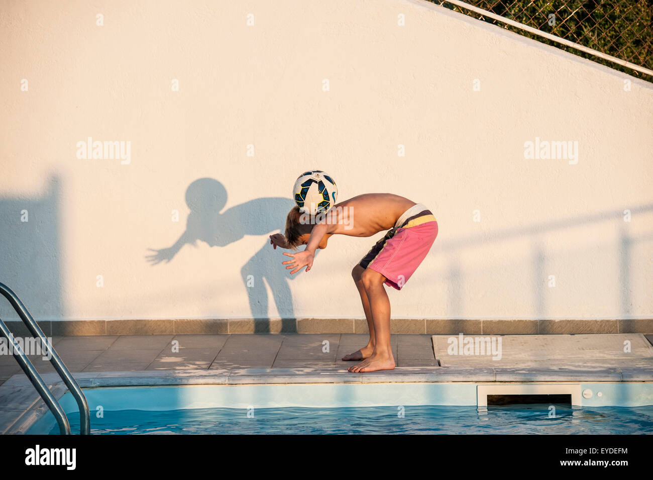 A boy playing football on holiday by a swimming pool Stock Photo - Alamy